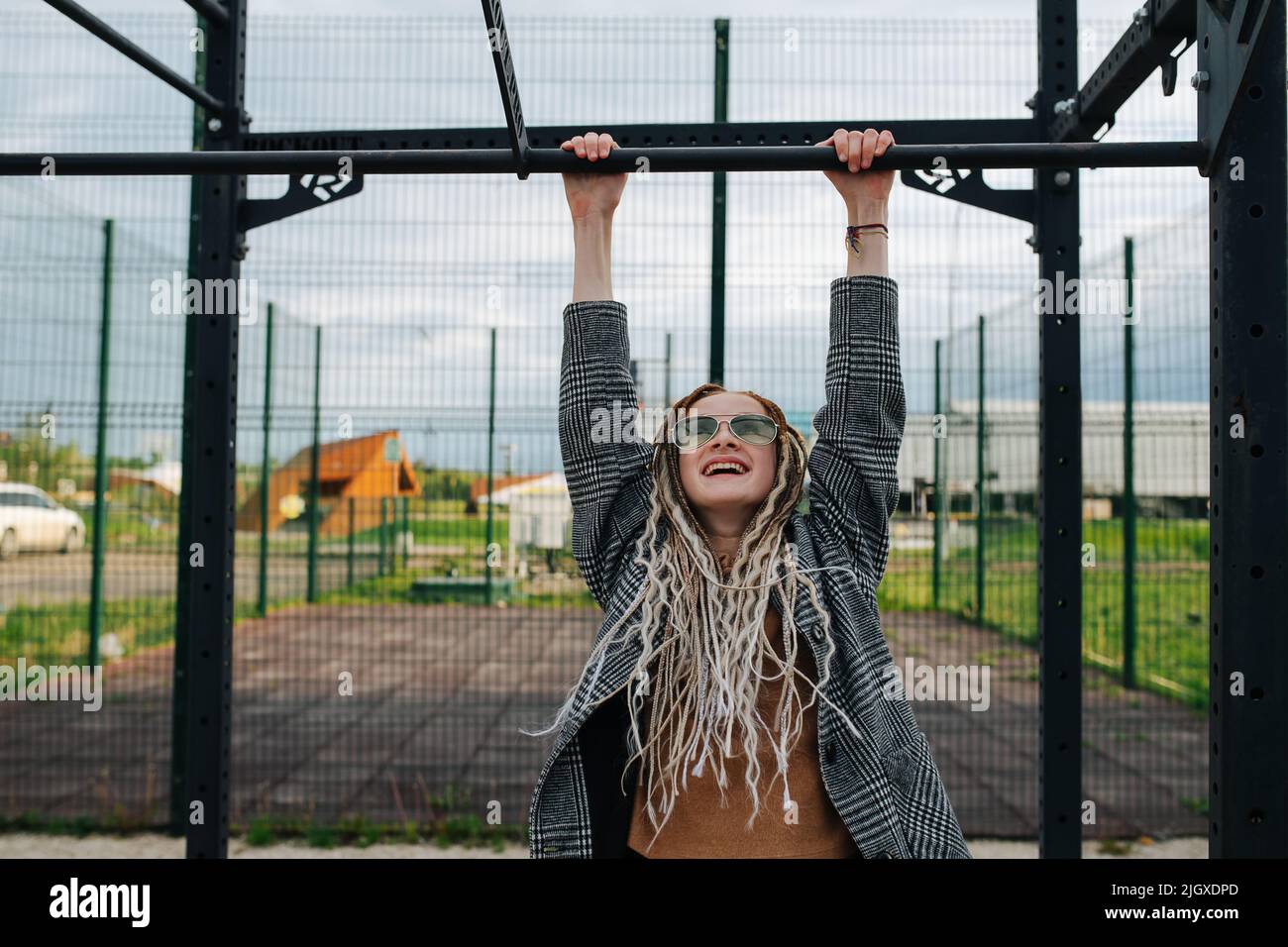Laughing teenage girl with dreads hanging on a high bar on the ...