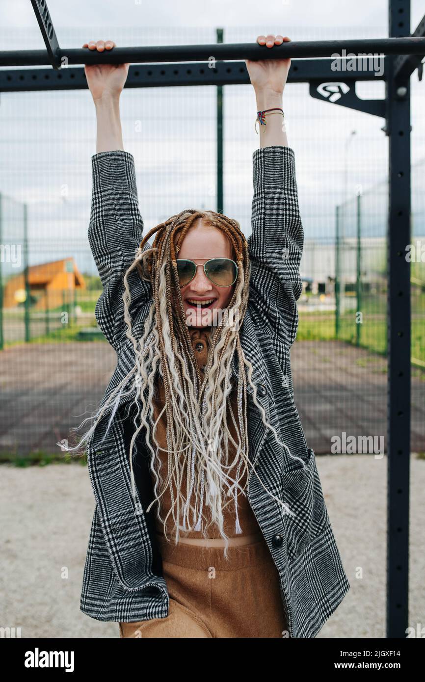 Optimistic teenage girl with dreads hanging on a high bar on the ...