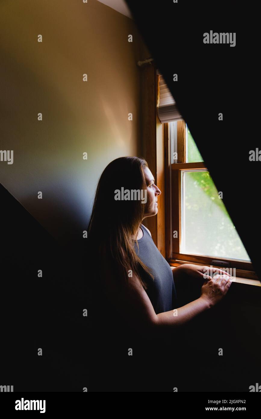 Woman looking out of a window in a dark room in the daytime Stock Photo ...