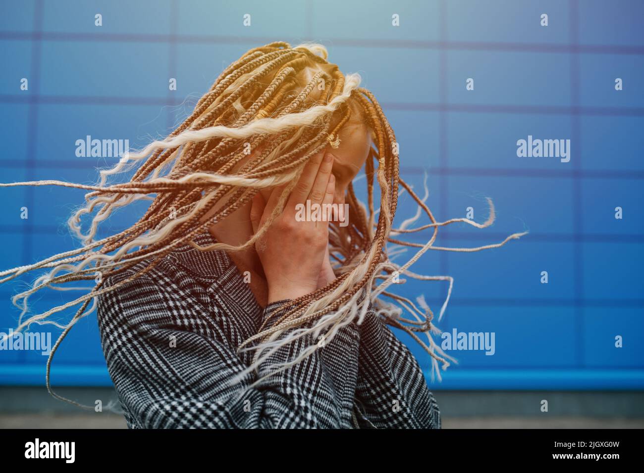 Dreads shaking lighthearted teenage girl in front of a blue panel wall ...