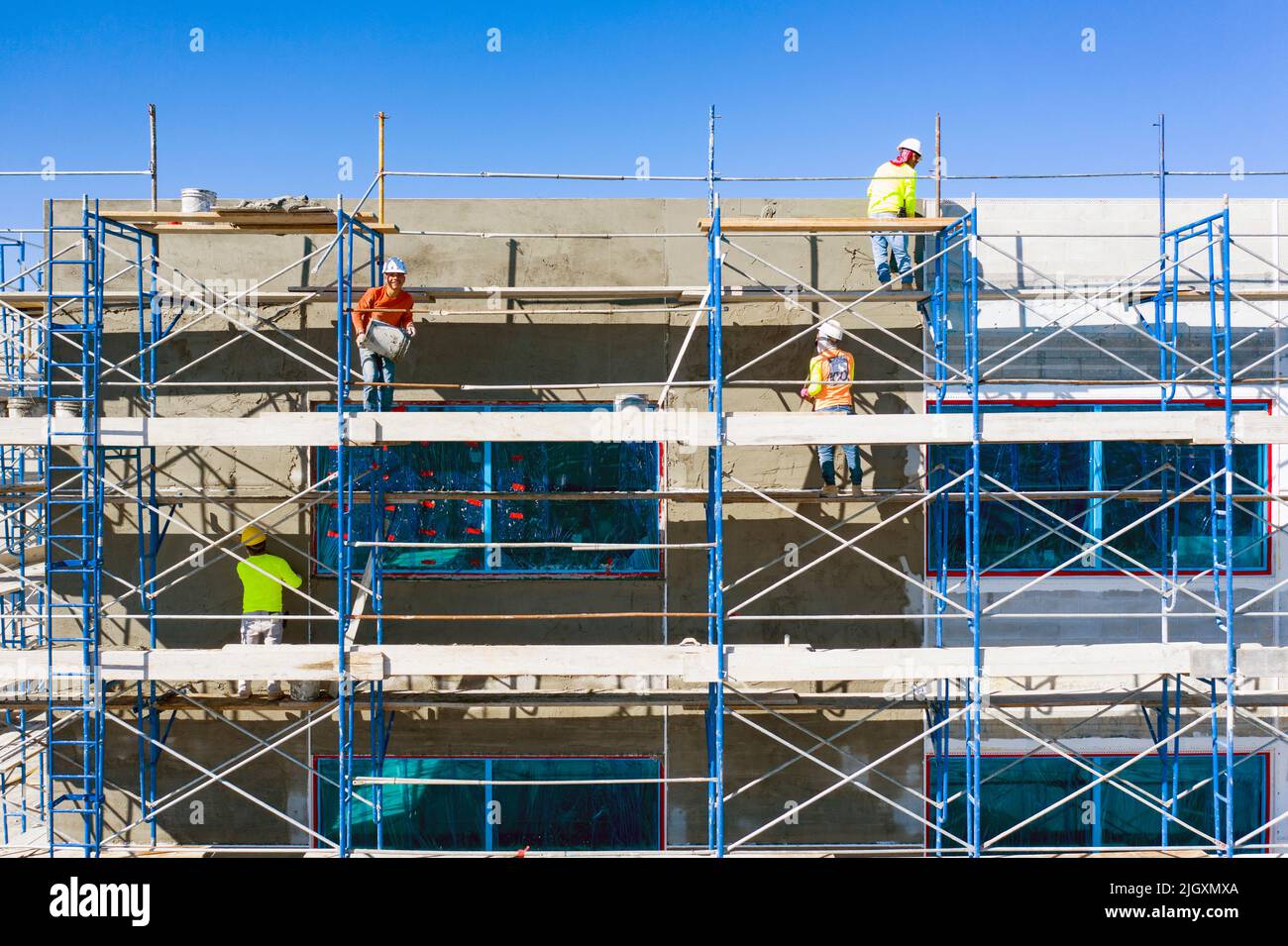 Four construction workers on scaffolding installing stucco to the ...