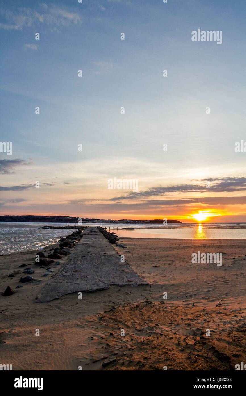 A vertical shot of a pier in a sandy beach at sunset and the Sun ...