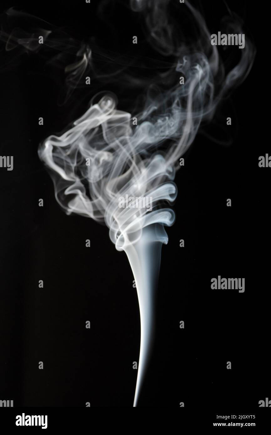 Puffs and curls of white smoke against a black background rising from a ...
