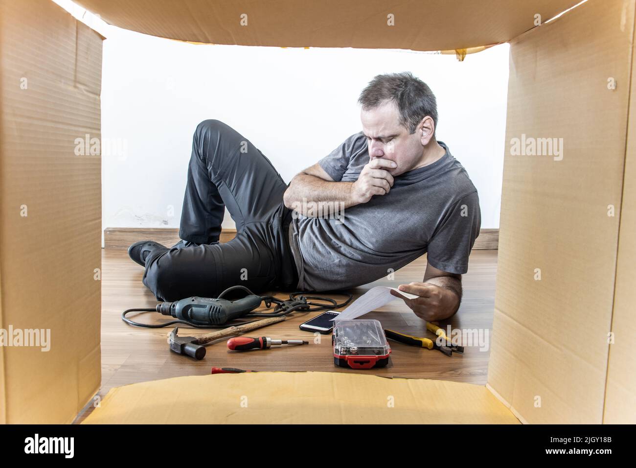 The man is lying on the floor with the tools around and thoughtfully ...