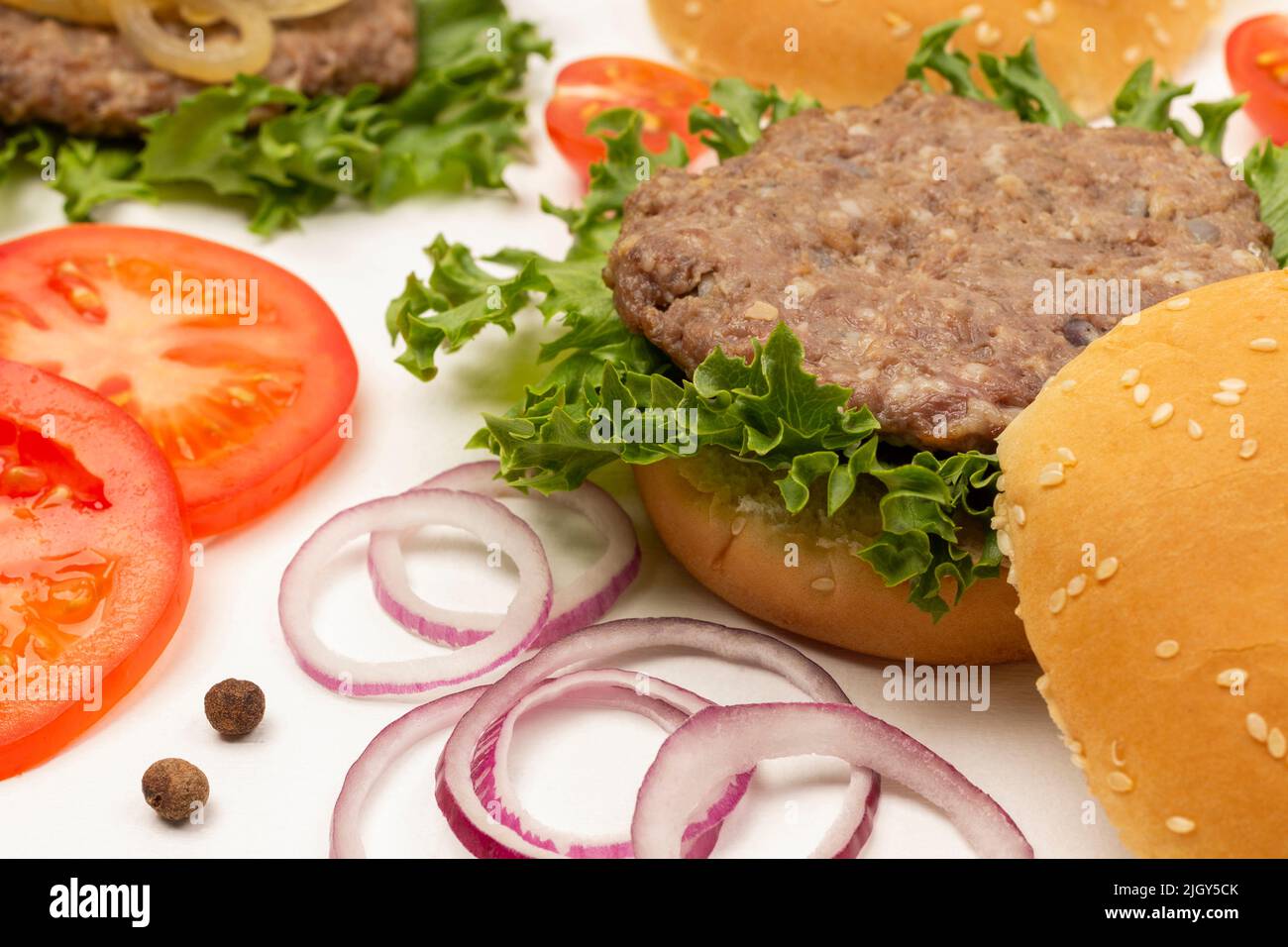 Burger bun on lettuce leaf. Chopped tomatoes and onions on table. Top ...