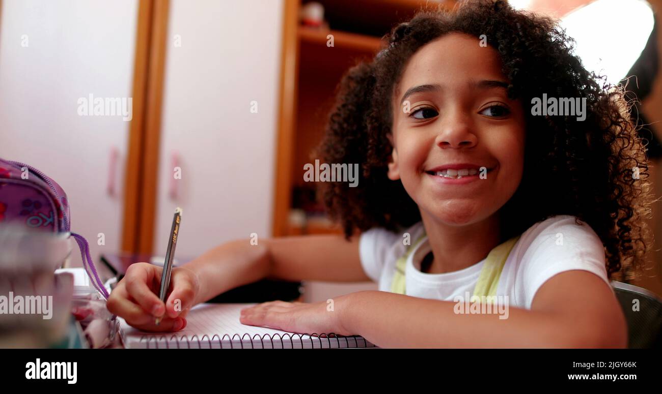 Cute schoolgirl smiling at camera while doing homework Stock Photo - Alamy