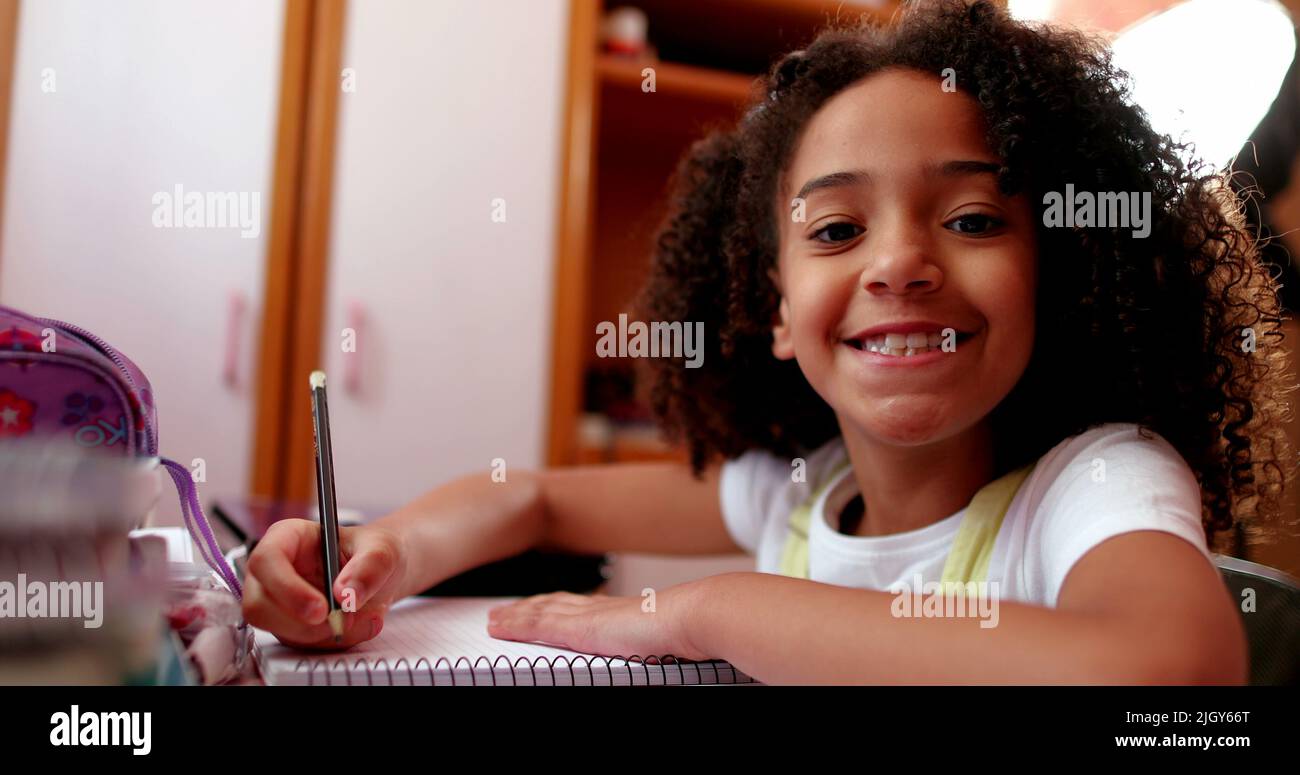 Cute schoolgirl smiling at camera while doing homework Stock Photo - Alamy