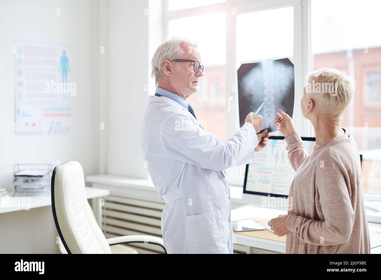 Serious senior male radiologist in white coat standing in own office ...