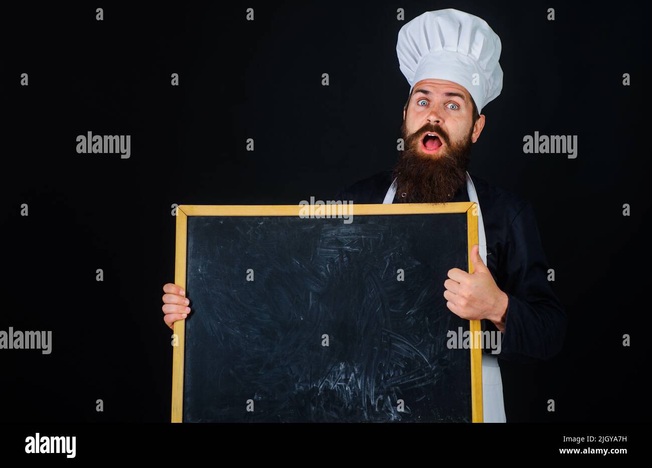 Surprised chef, cook or baker in uniform with empty menu chalkboard ...