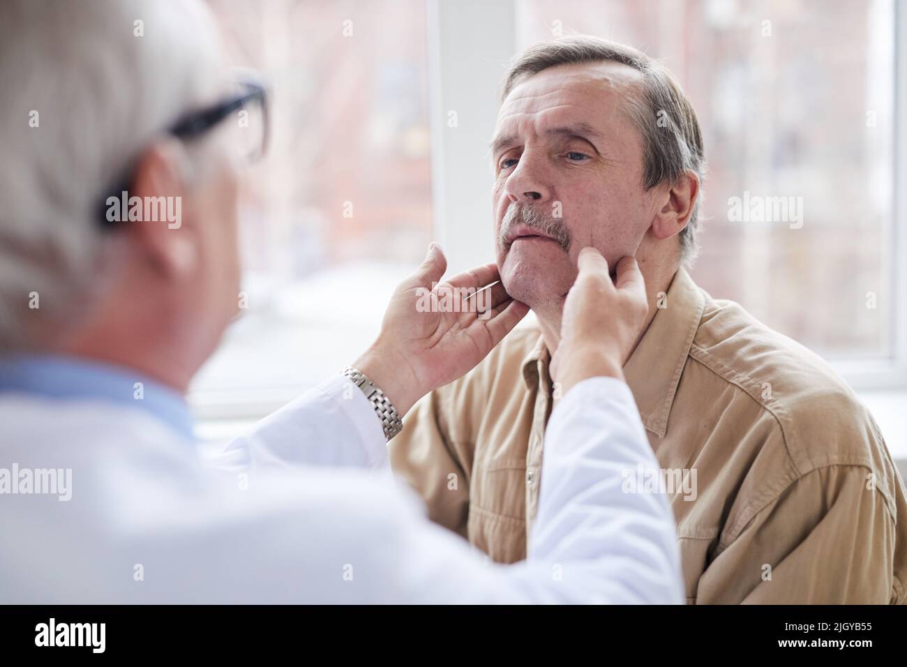Over shoulder view of doctor checking lumps on neck of aged male ...