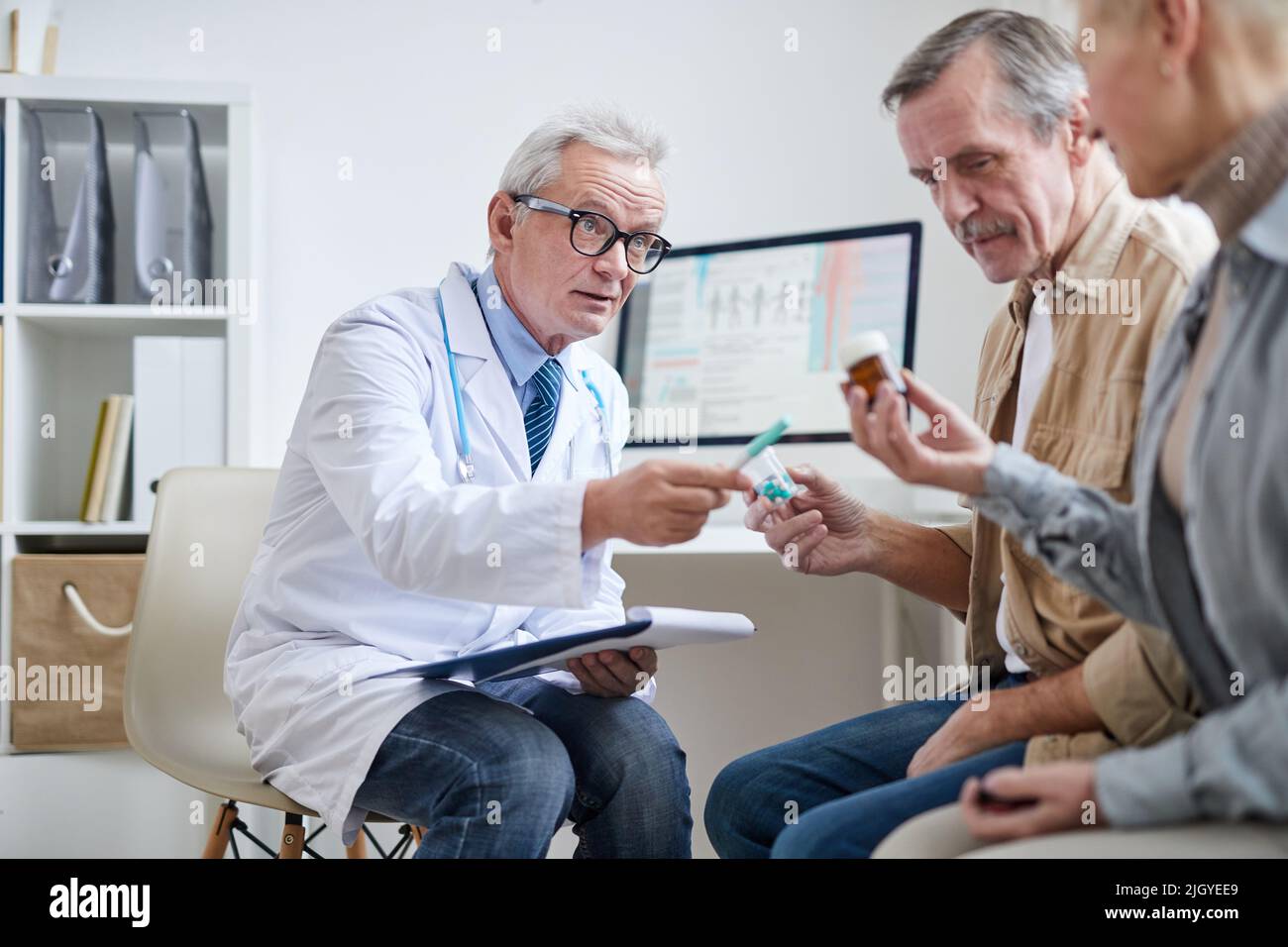 Senior gray-haired doctor with stethoscope around neck pointing at pill ...