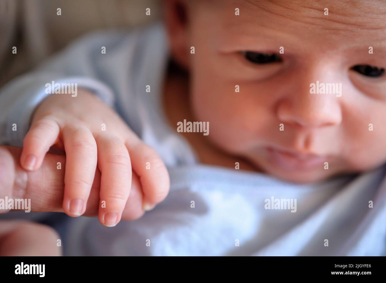 Close-up detail macro view of baby holding on to mom's finger with his ...