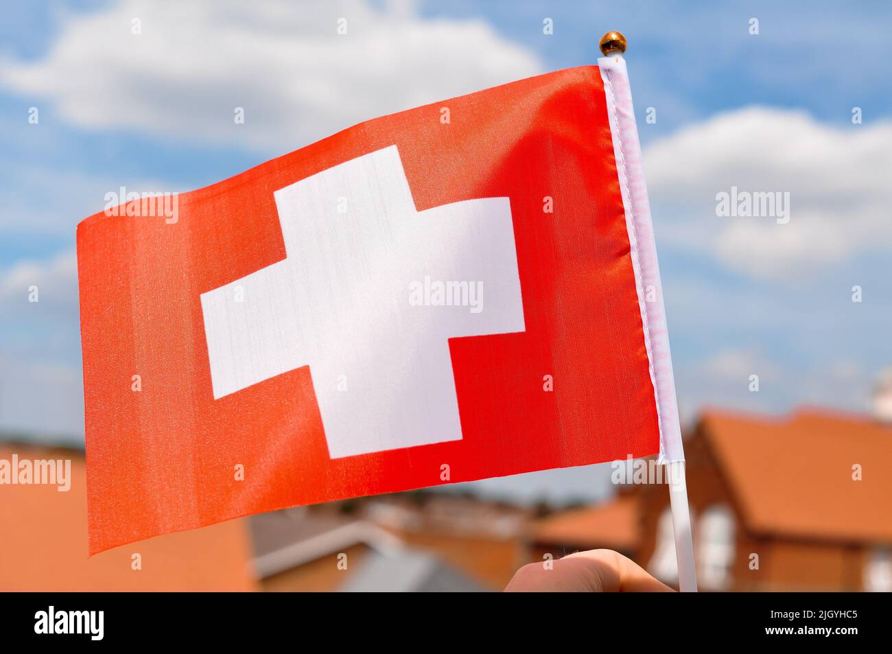national red flag with white cross of Switzerland close up in blue sky ...