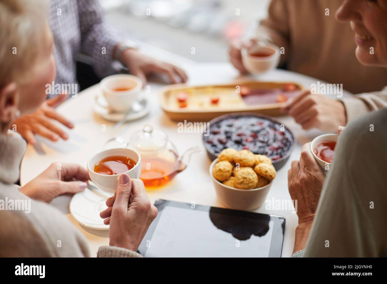 Over shoulder view of seniors sitting at table with tablet and drinking ...
