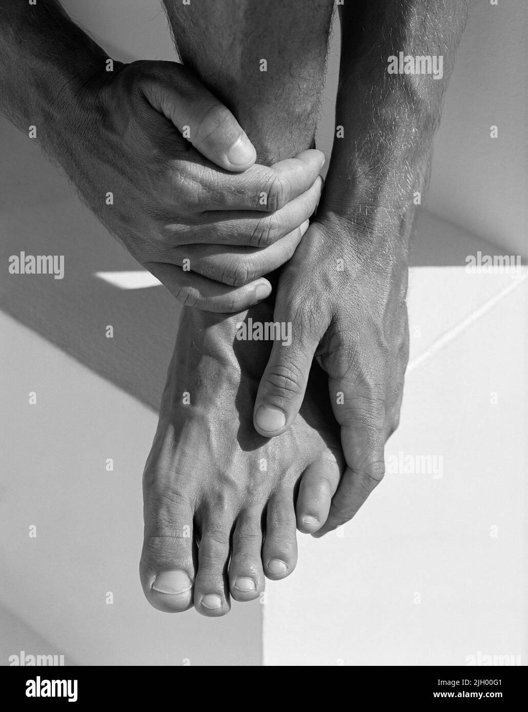 a closeup grayscale of a man's hands touching his foot Stock Photo - Alamy
