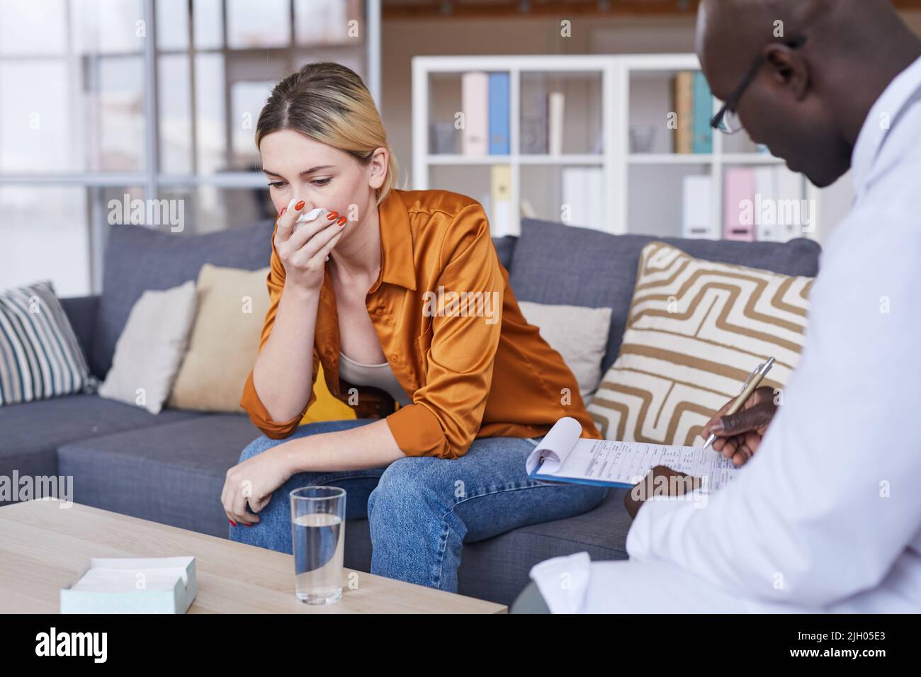 Grief-sicken young woman in casual outfit sitting on sofa and covering ...