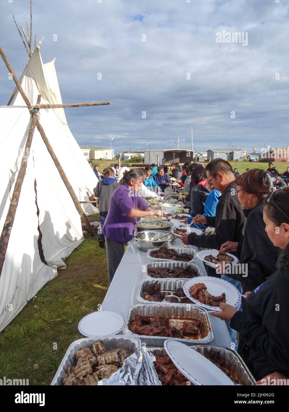 Indigenous people lined up at community feast in the summer, in the ...