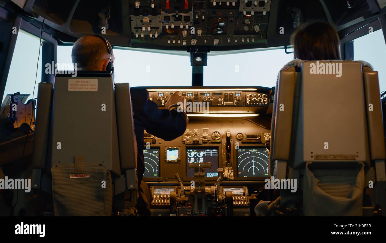 Captain And Woman Copilot In Cockpit Preparing To Fly Airplane Using Dashboard Command Buttons