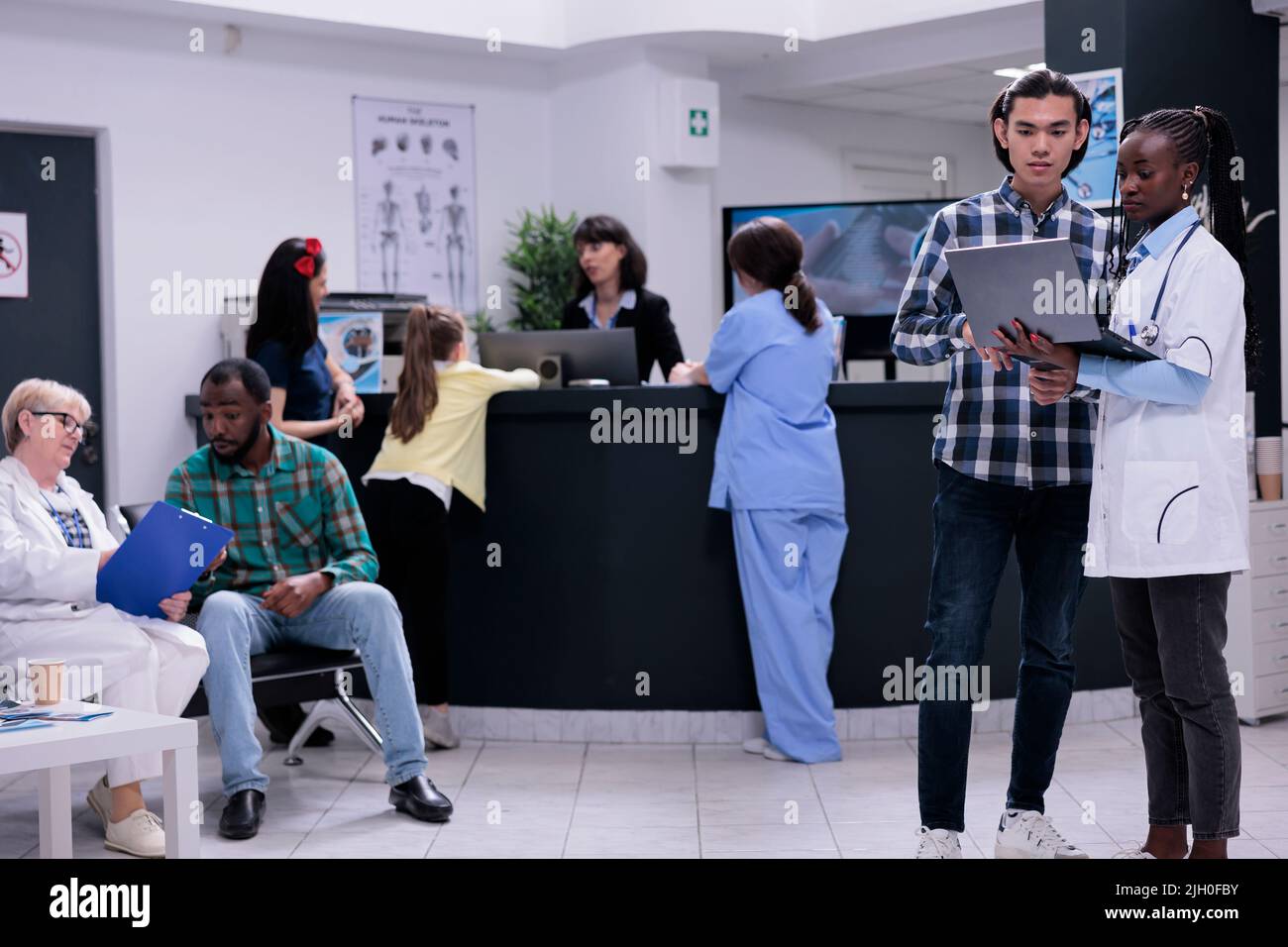 Medic holding laptop with lab results talking with asian patient while ...