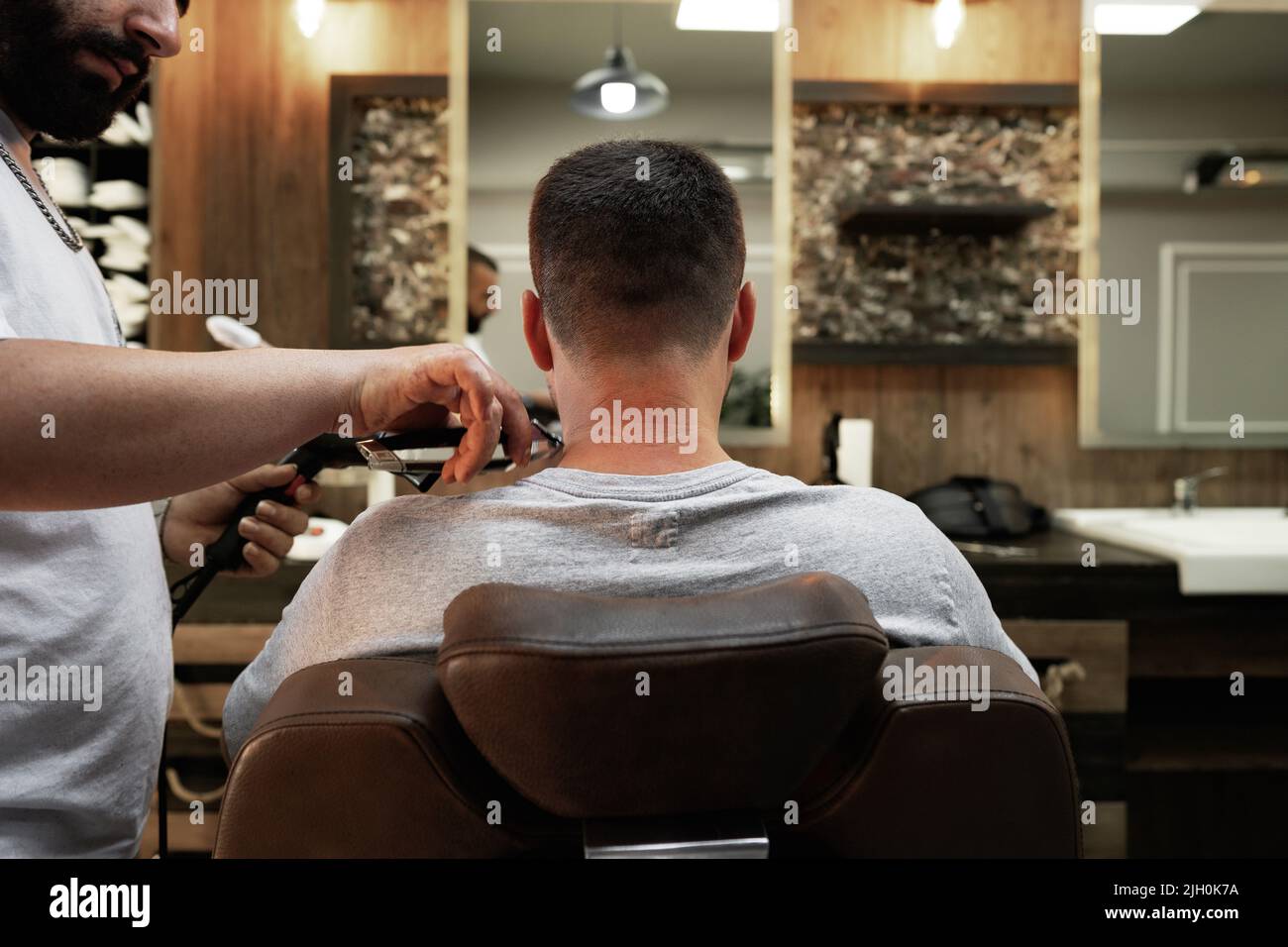 Barber guy gives a haircut to a bearded man sitting in a chair in a ...