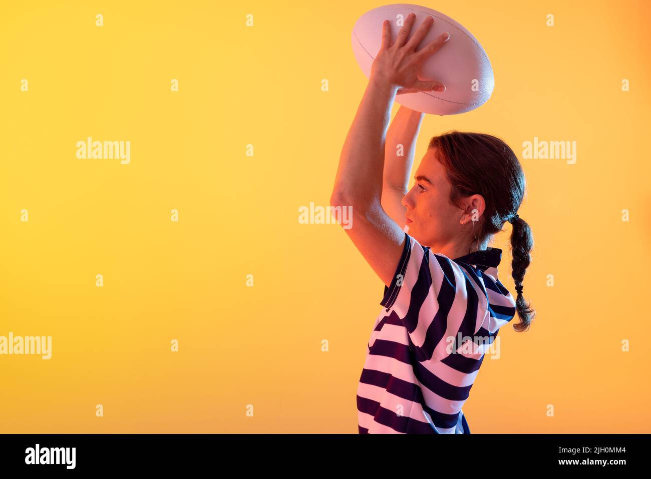 Caucasian female rugby player with rugby ball over neon yellow lighting ...