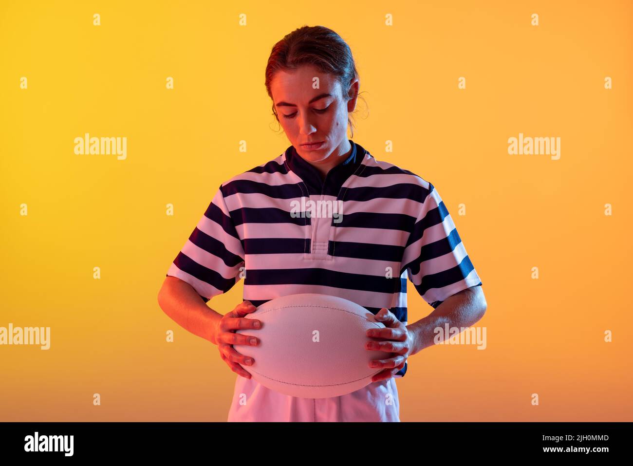 Caucasian female rugby player with rugby ball over neon yellow lighting ...