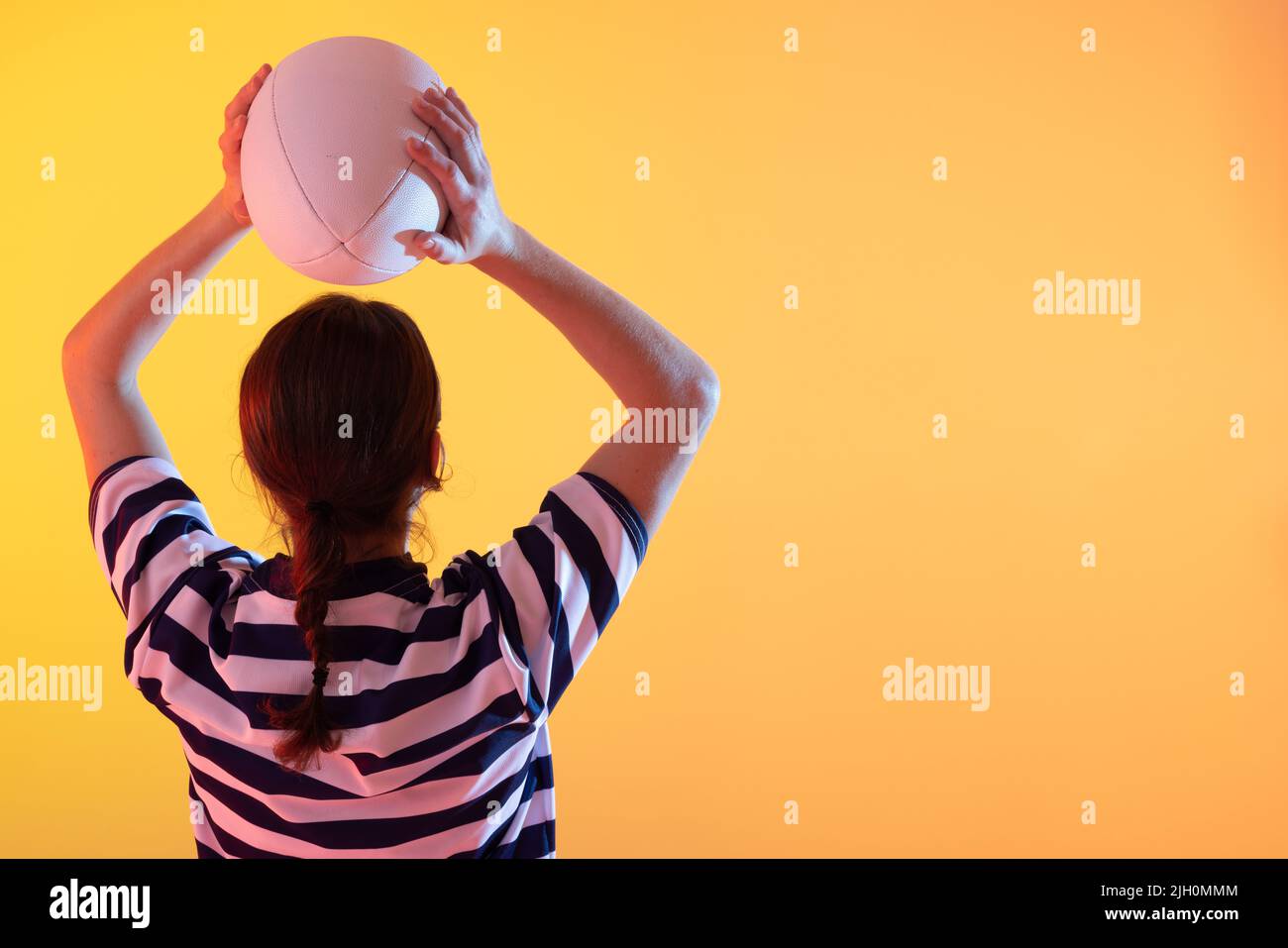 Rear view of caucasian female rugby player with rugby ball over neon ...