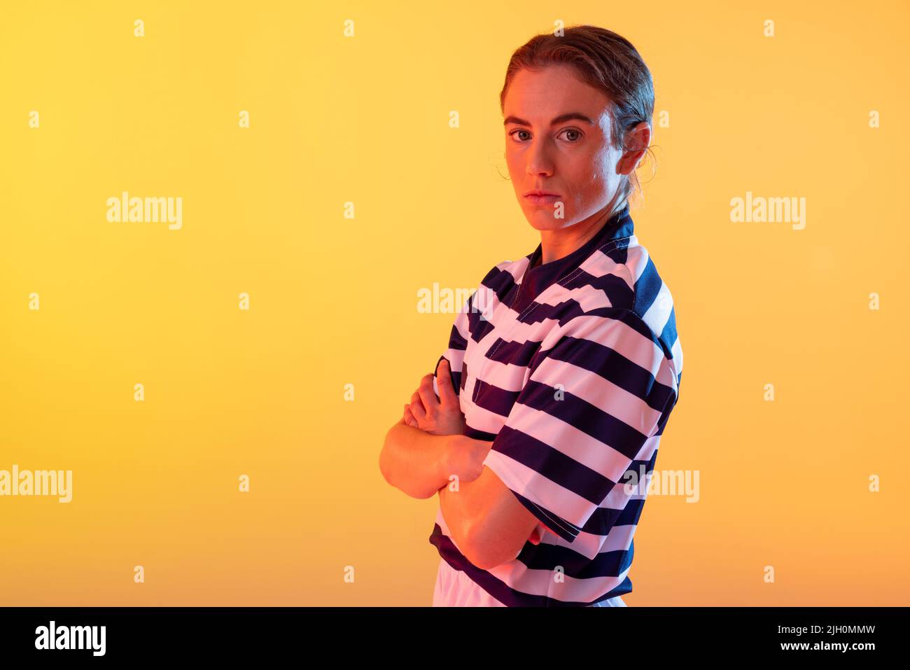 Portrait of caucasian female rugby player with arms crossed over neon ...