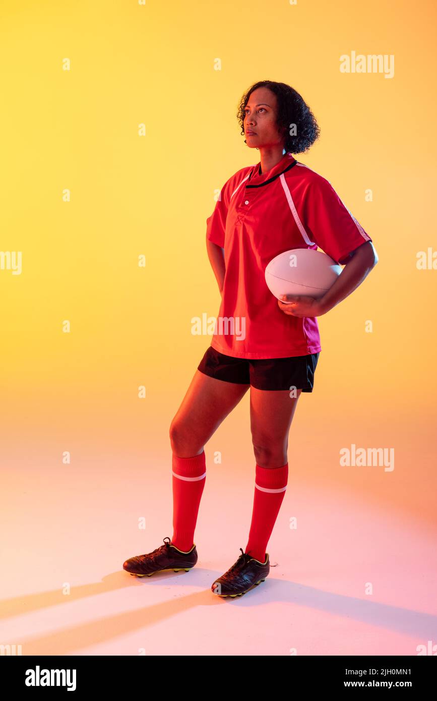 African american female rugby player with rugby ball over neon yellow ...