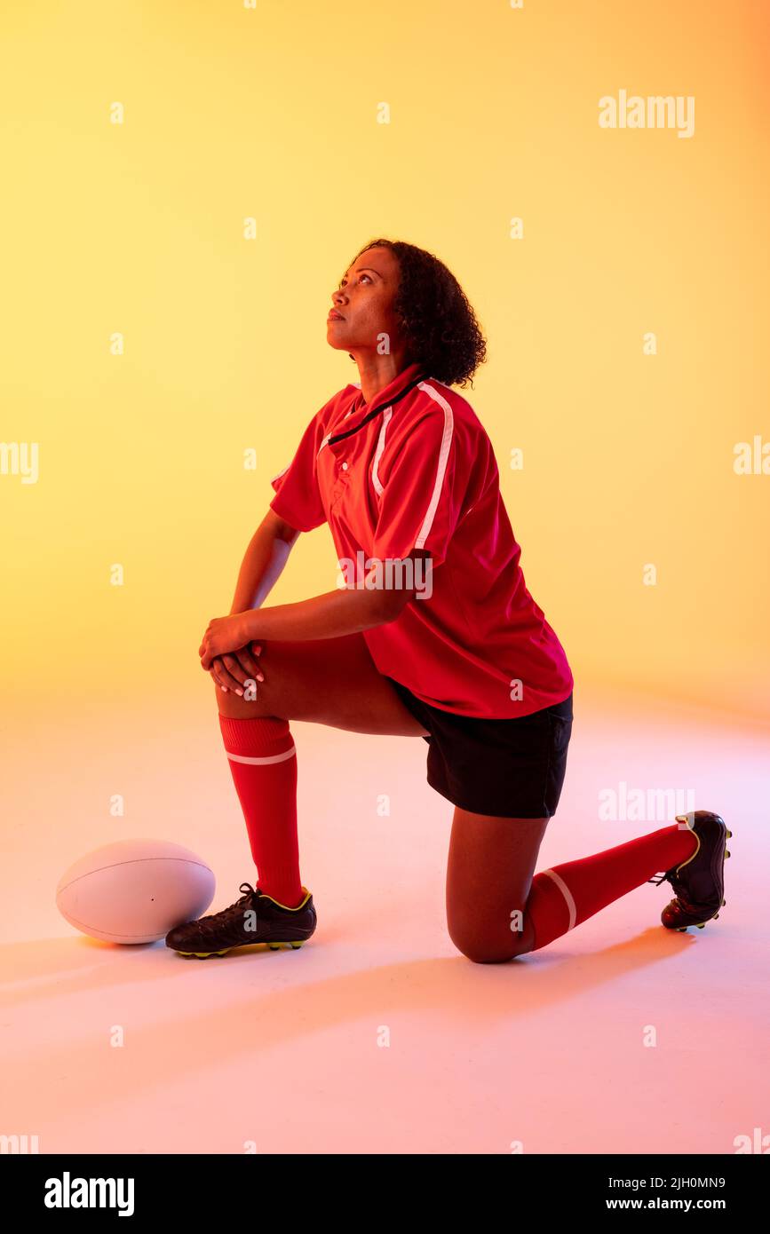 African american female rugby player with rugby ball over neon yellow ...