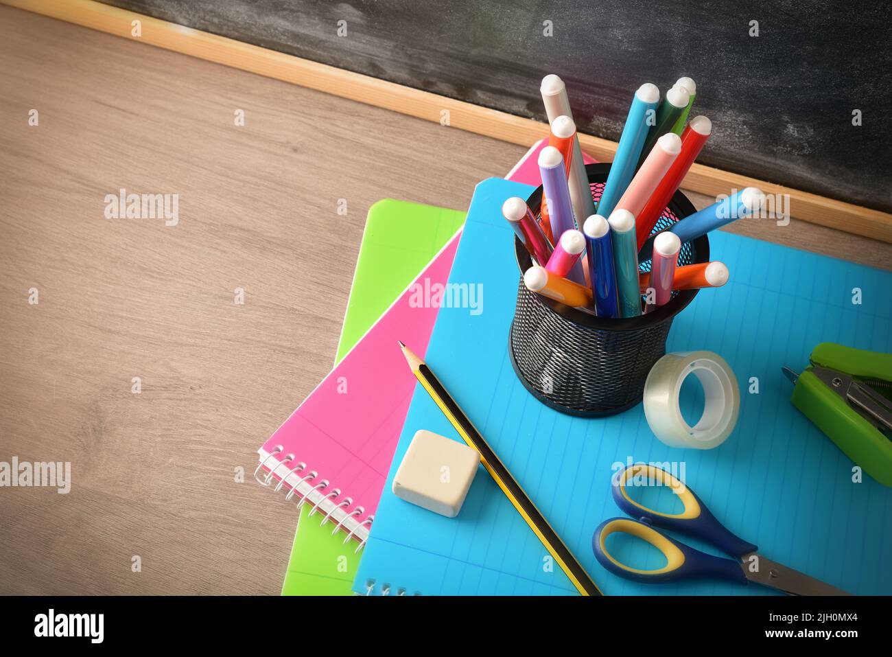 School supplies with pen with markers on notebooks with tools on wooden desk and blackboard ...