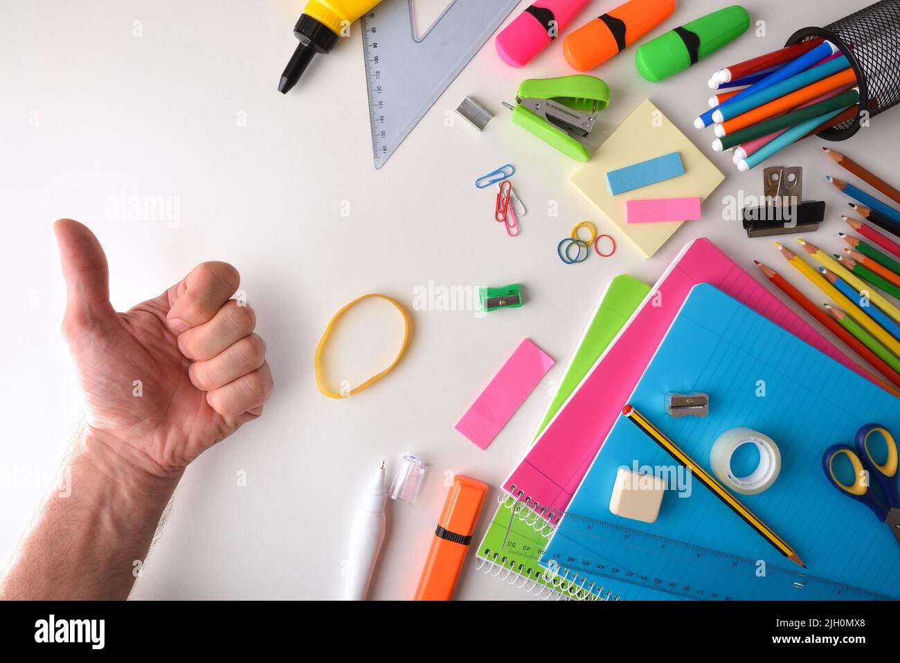 Assortment of colorful school supplies on white desk and hand with ok ...