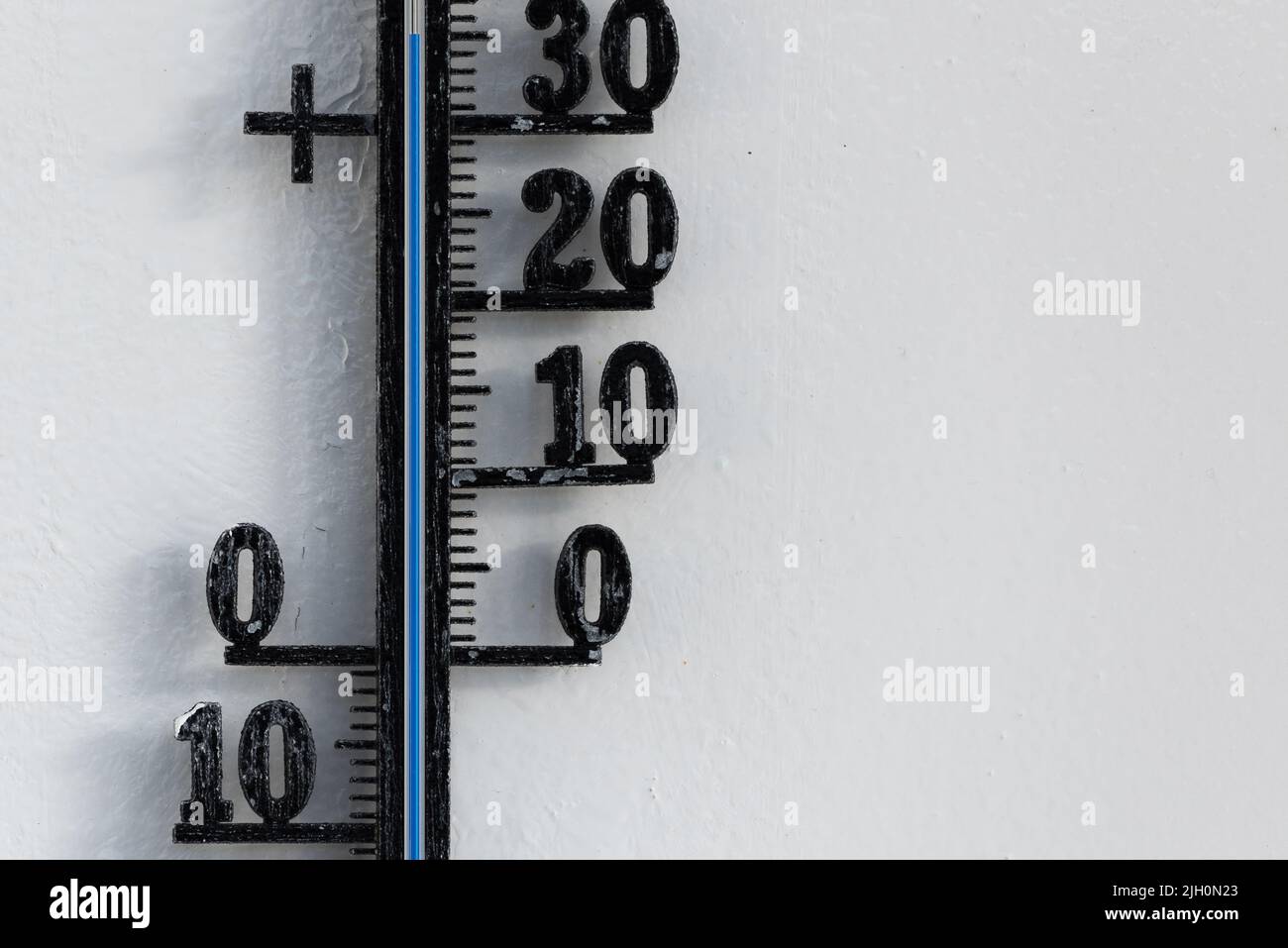 Classic black analog thermometer hanging on white wall displaying blue ...
