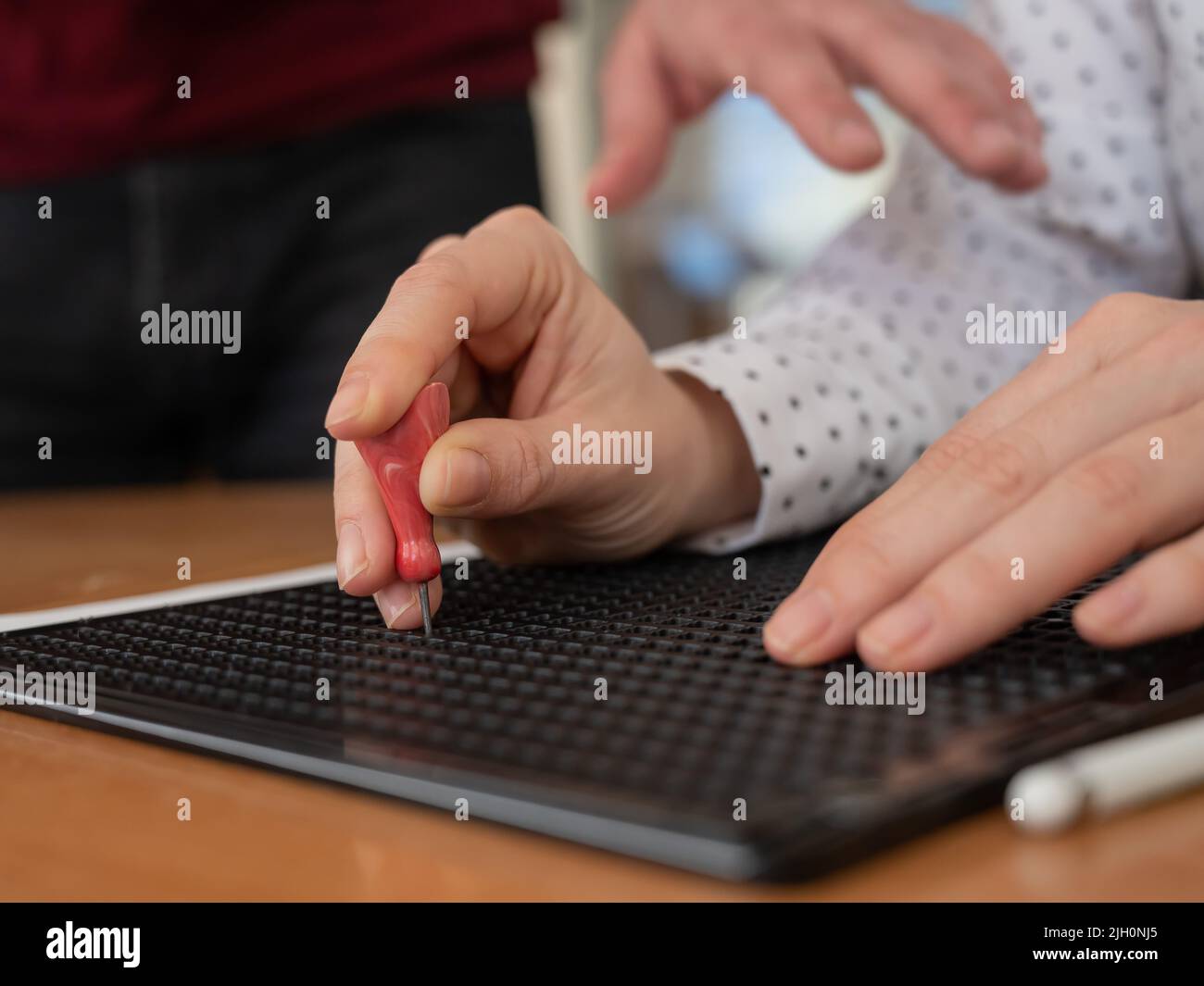 A man teaches a woman how to use a special stencil and stylus to write ...