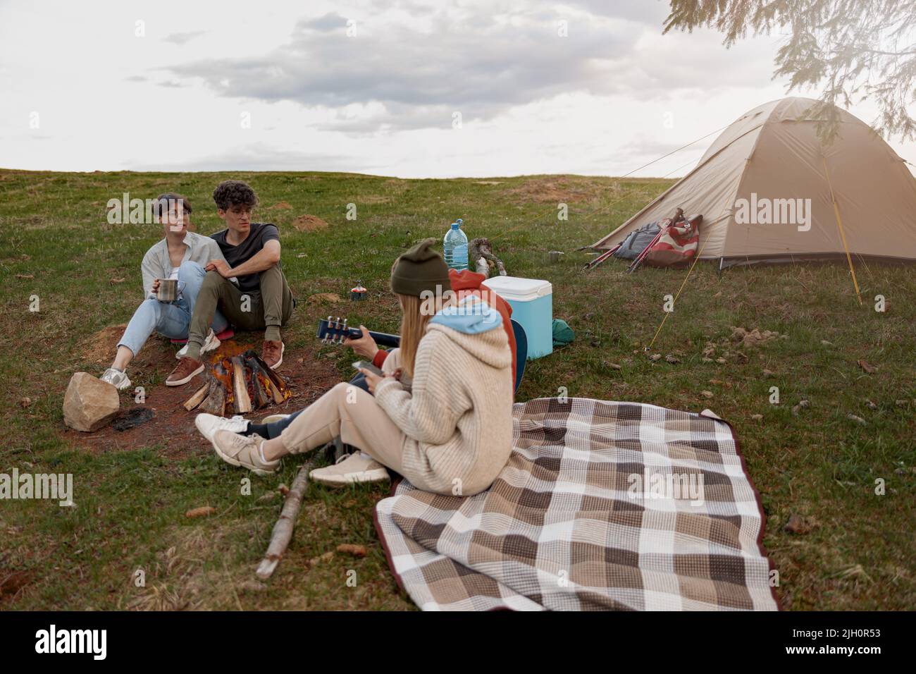 Young people hanging out at fire in camp site high in mountains ...