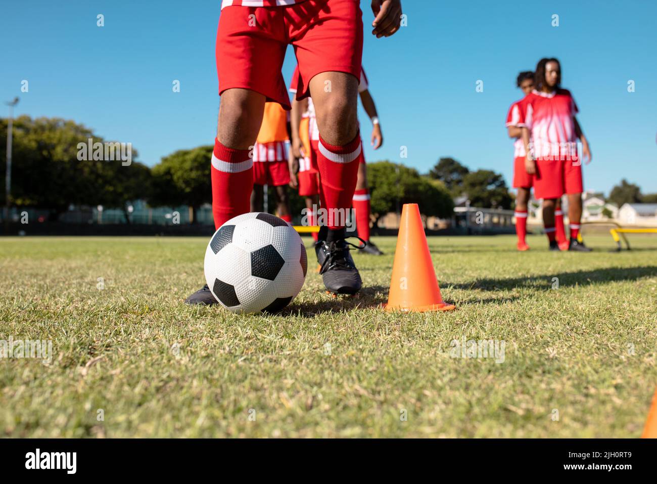 Low section of male multiracial players dribbling ball between cones at ...
