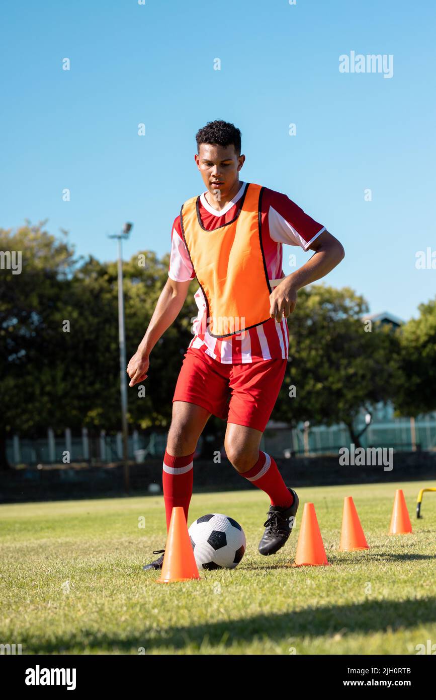Biracial male player in red jersey running with soccer ball between ...