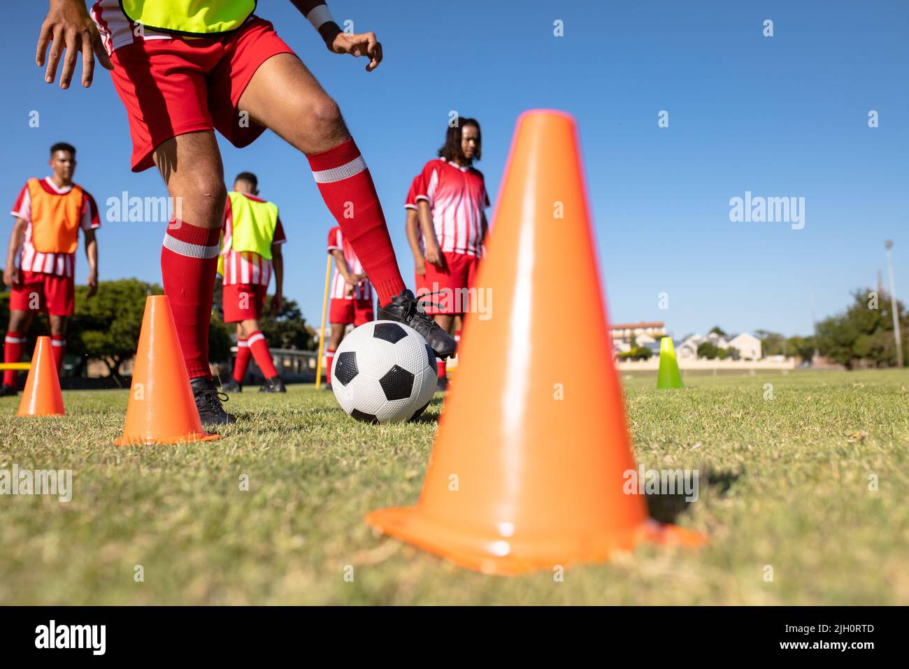 Multiracial male soccer players dribbling ball between oranges cones ...