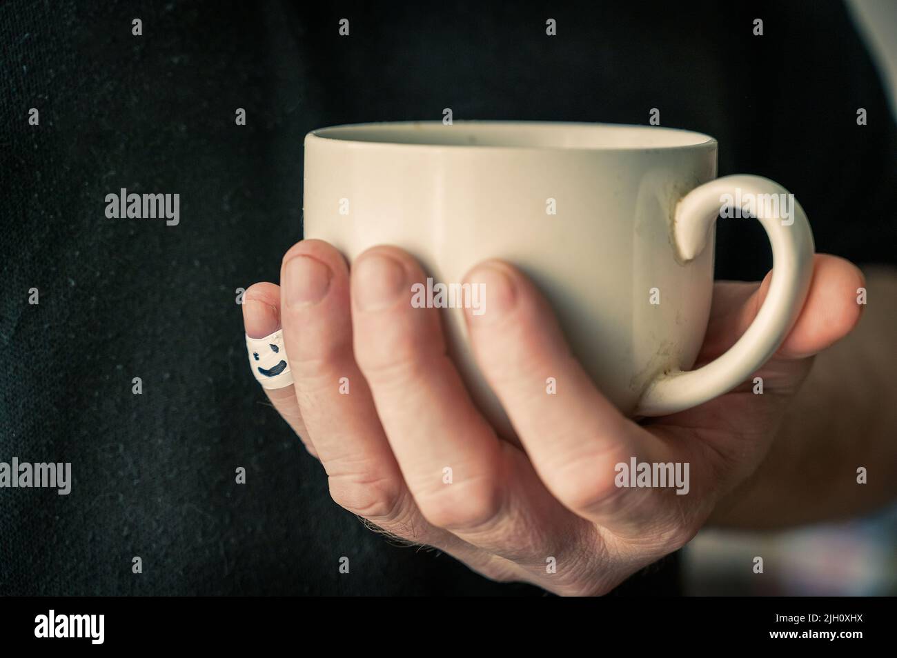 A man is holding a ceramic cup in his hand. The first phalanx of his ...