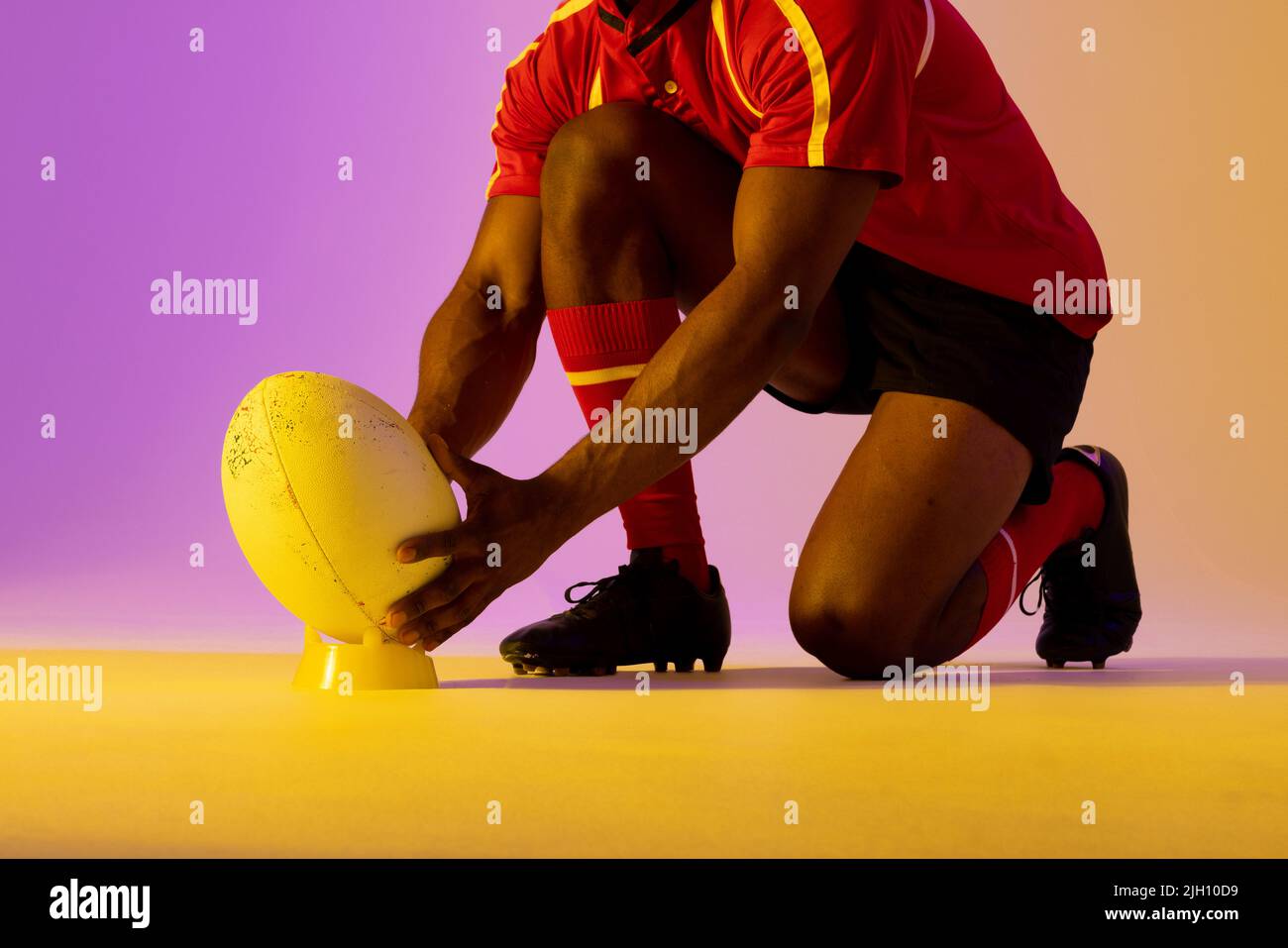 African american male rugby player crouching with rugby ball over pink ...