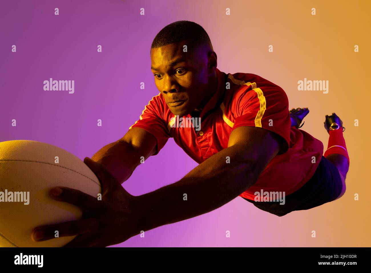African american male rugby player jumping with rugby ball over pink ...