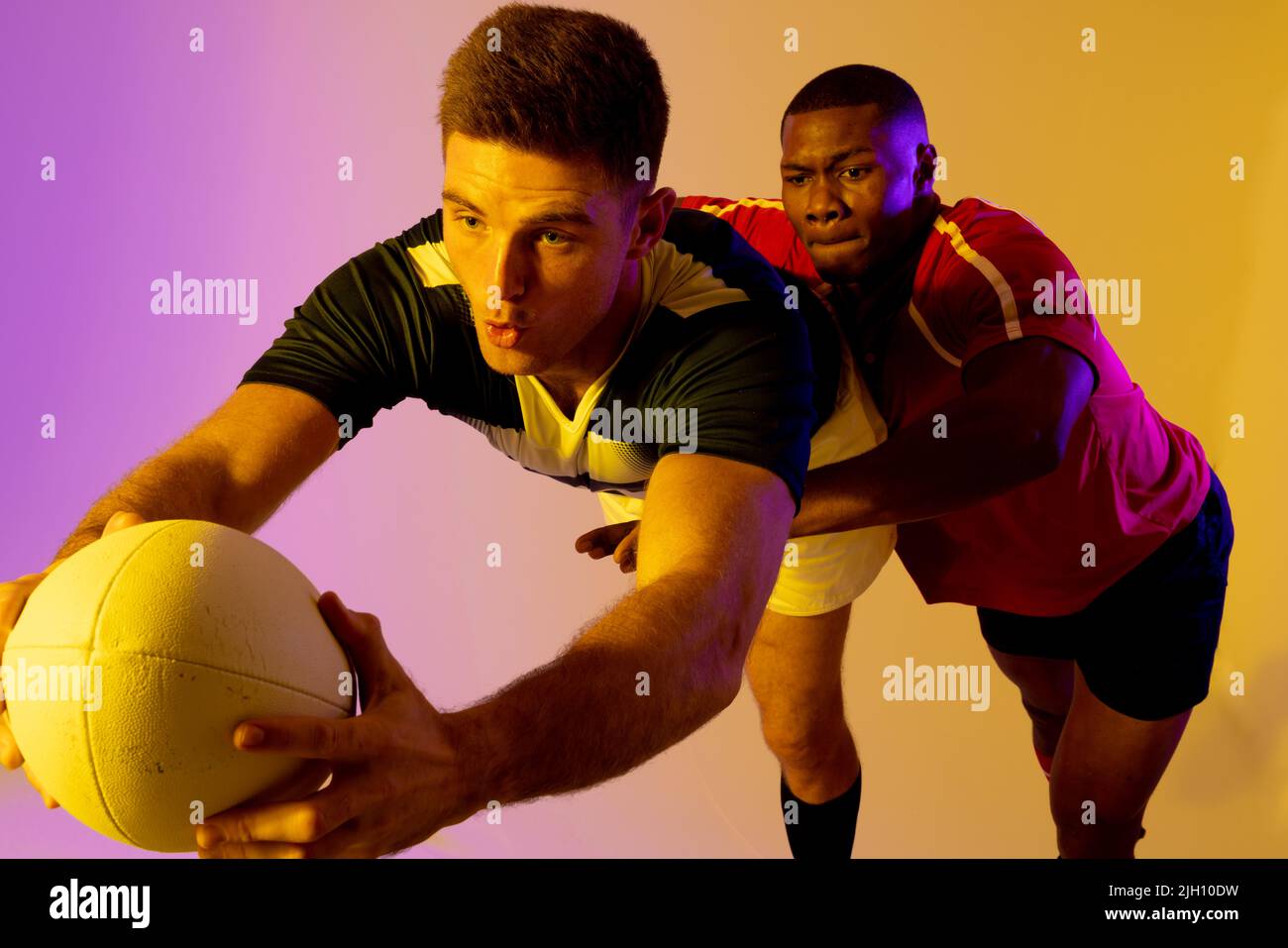 Diverse male rugby players with rugby ball playing over pink lighting ...