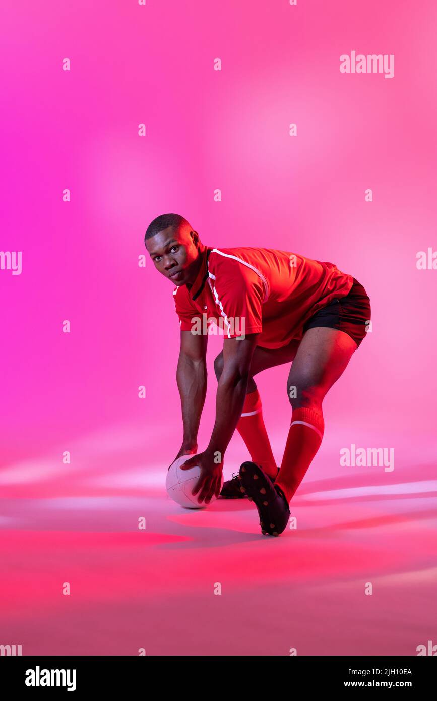 African american male rugby player catching rugby ball over pink ...