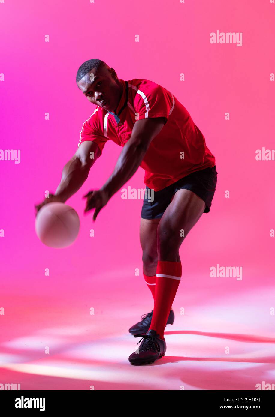 African american male rugby player catching rugby ball over pink ...