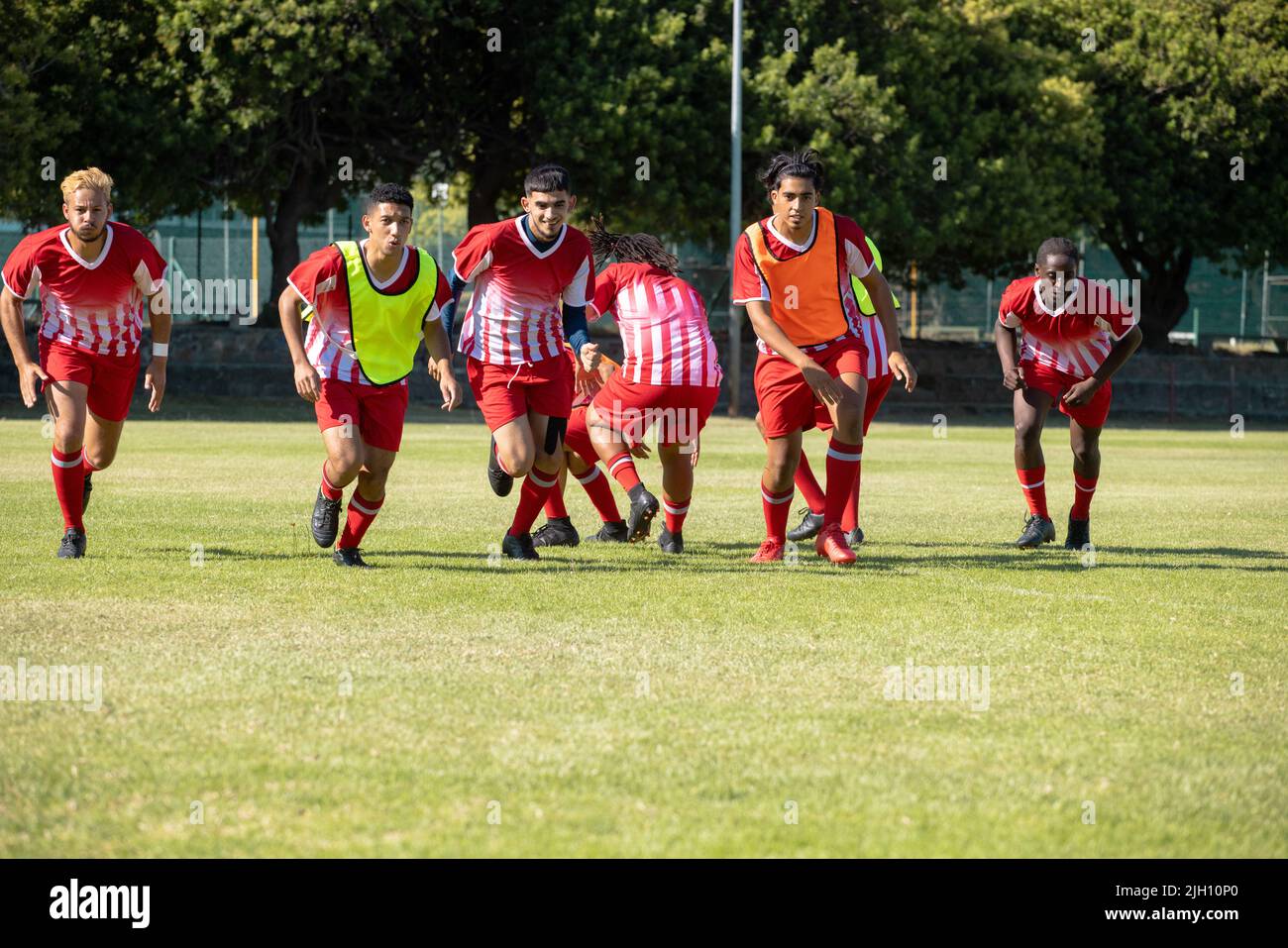 Multiracial male soccer players wearing red sports uniforms running on ...