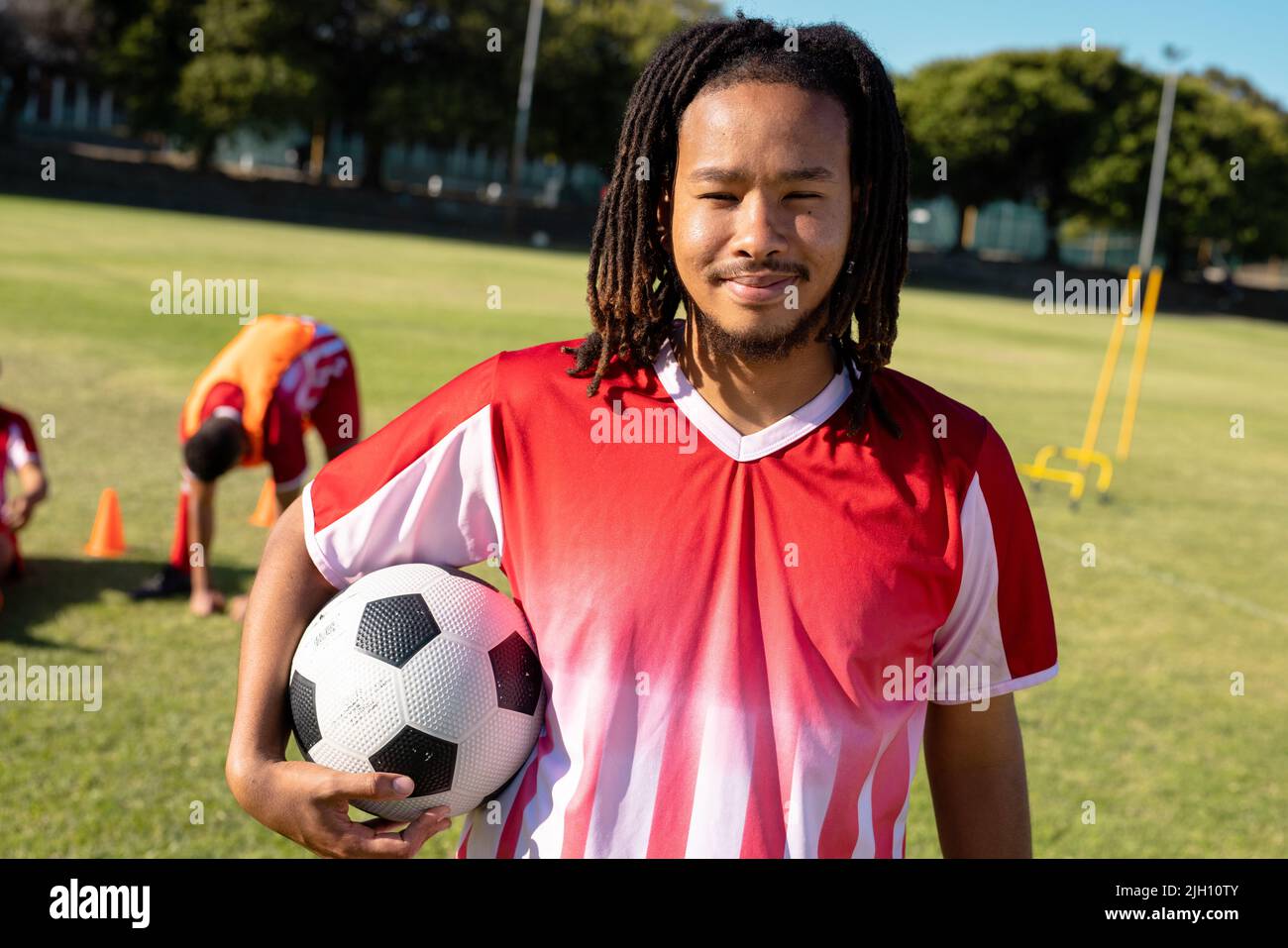 Portrait of biracial smiling male player with dreadlocks holding soccer ...
