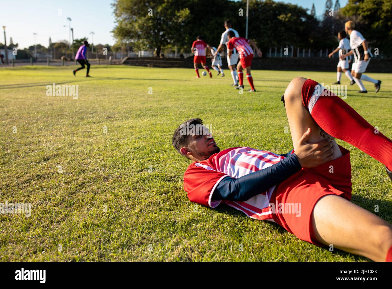 Multiracial player with physical injury lying on grassy field and ...