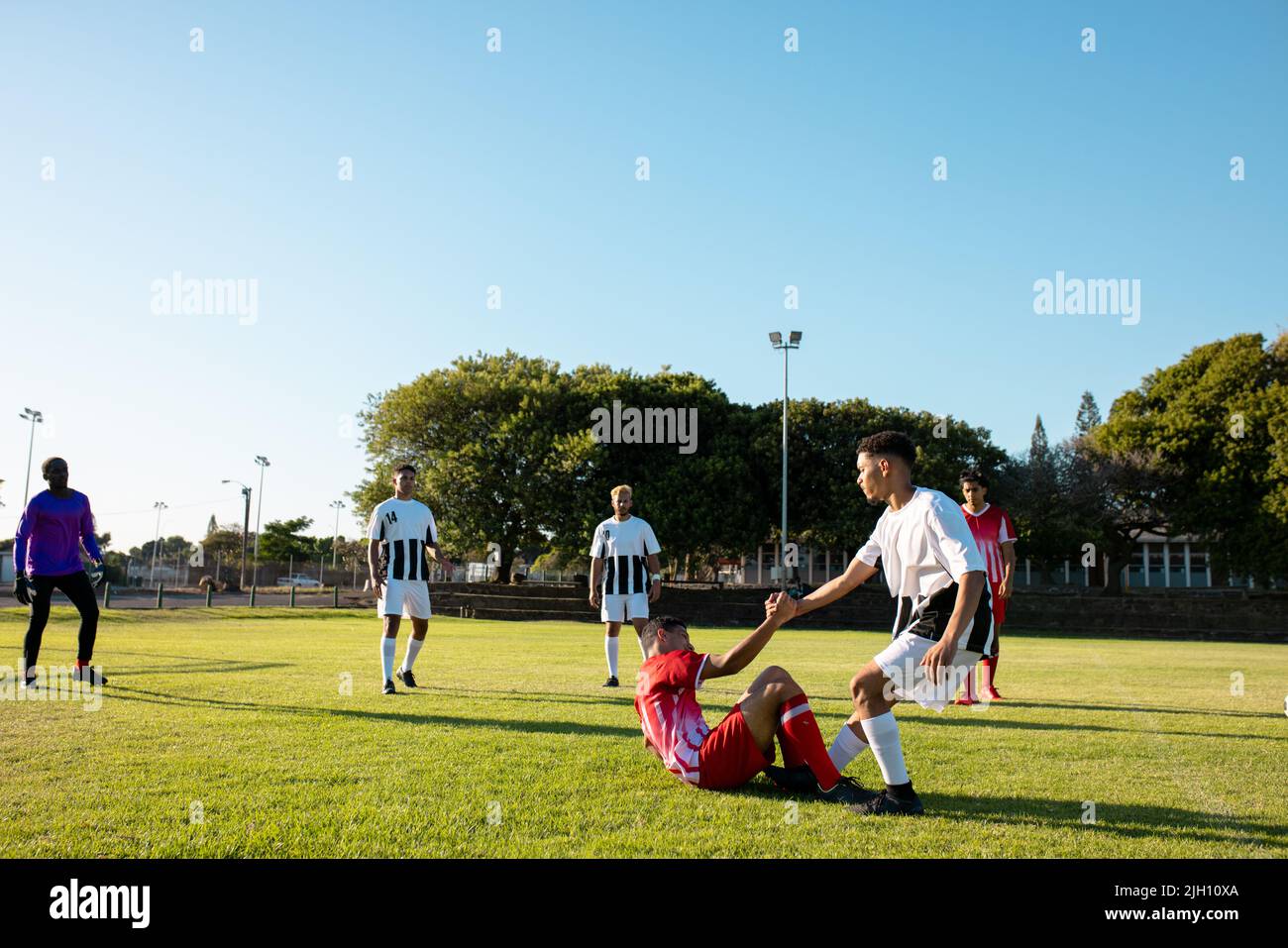 Multiracial player holding hand and assisting injured opponent to get ...