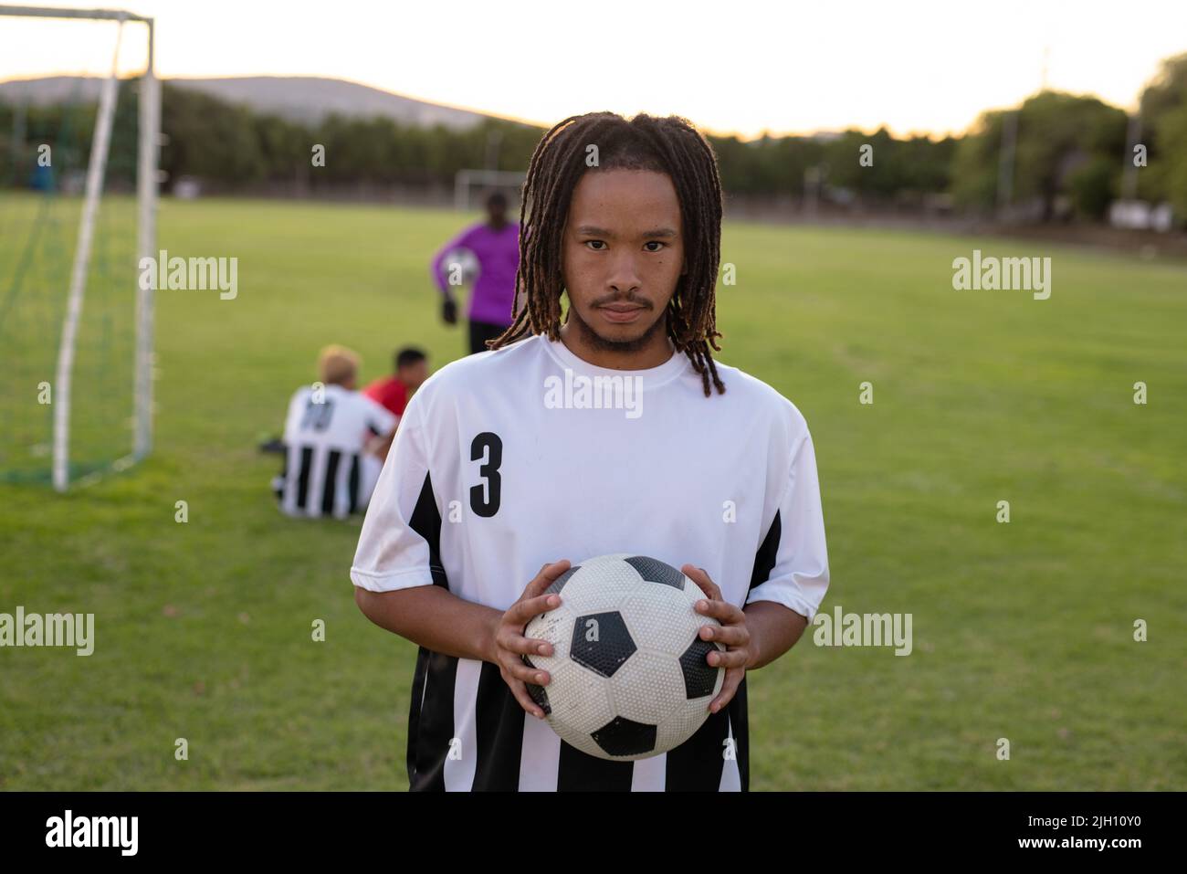 Portrait of serious biracial male player in white uniform holding ...