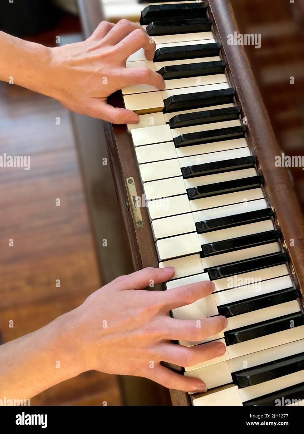 Hands on a brown piano with natural ivory keys and a reflective wood ...